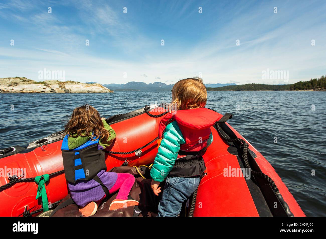 Two young kids sit at bow of rubber raft looking at rocky island Stock ...
