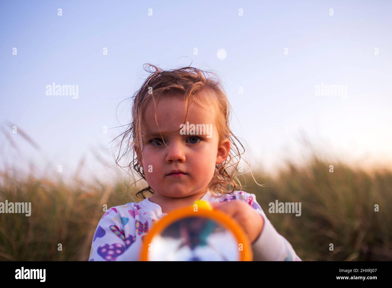 Young child holds flashlight and looks at camera with grasses behind ...