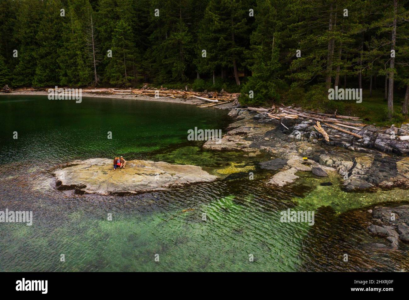 A family sits on rock surrounded by clear green water and forests Stock ...
