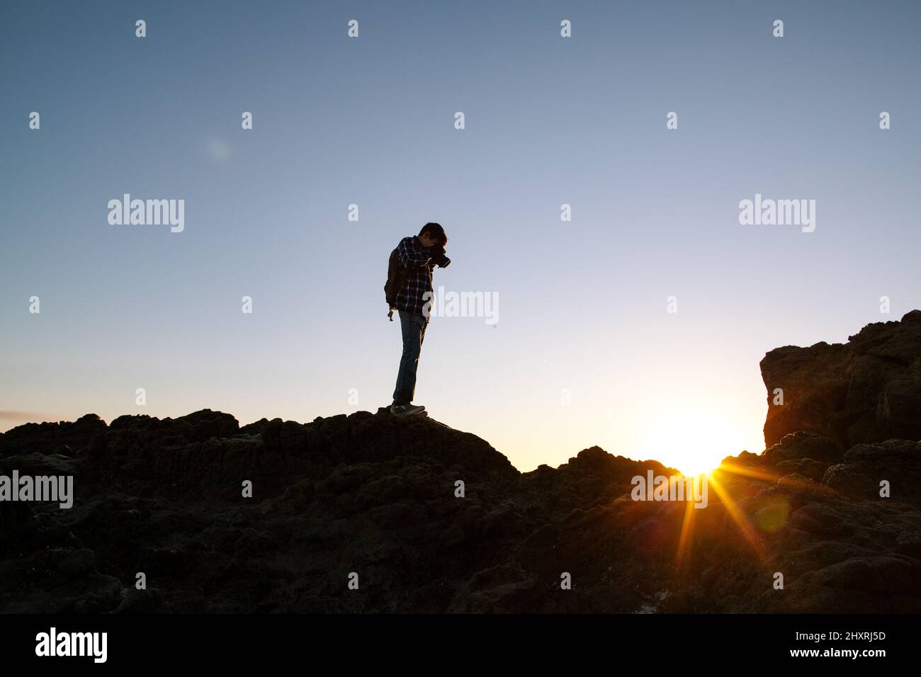Tween Boy Stands Backlit On A Rock While Taking A Picture Stock Photo ...