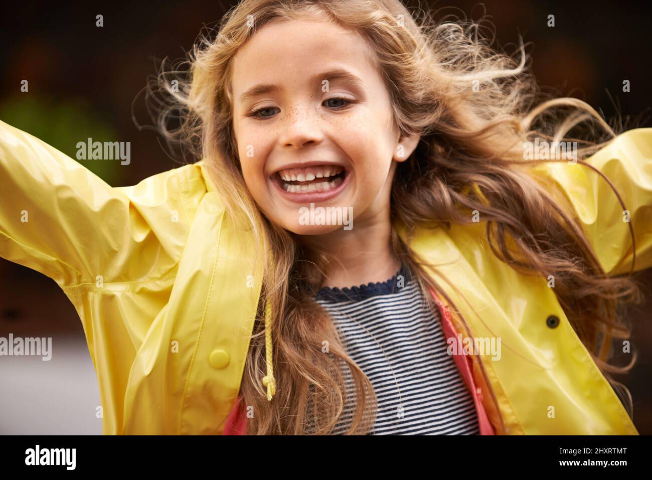 Squeal for joy. Shot of a cute little girl wearing a raincoat playing ...