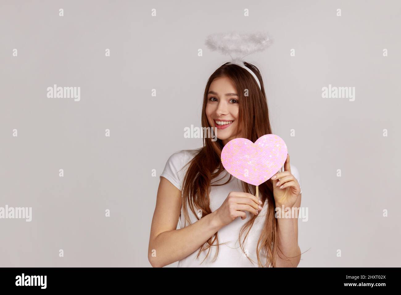 Angelic woman with holy nimbus holding pink paper heart on stick and ...