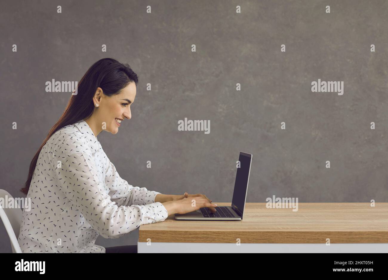 Side view of happy smiling young woman sitting at desk and working on ...