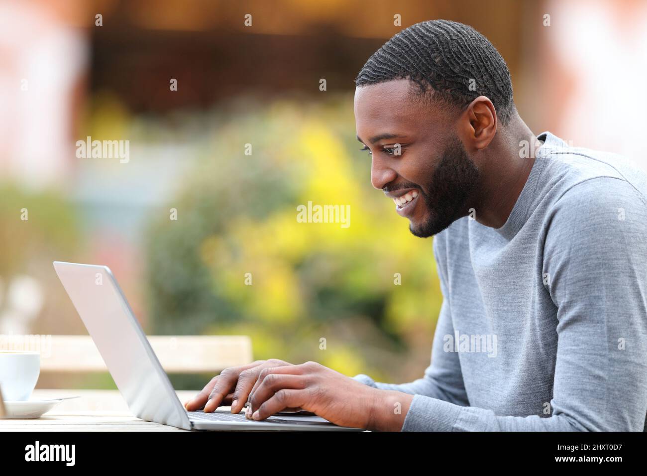 Side view portrait of a happy man with black skin using laptop in a bar ...