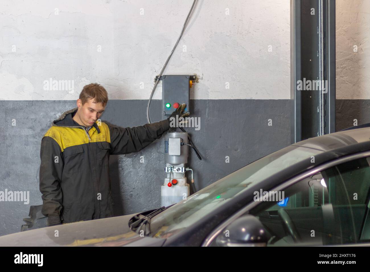 Hardworking man mechanic lifting car standing at the service station ...