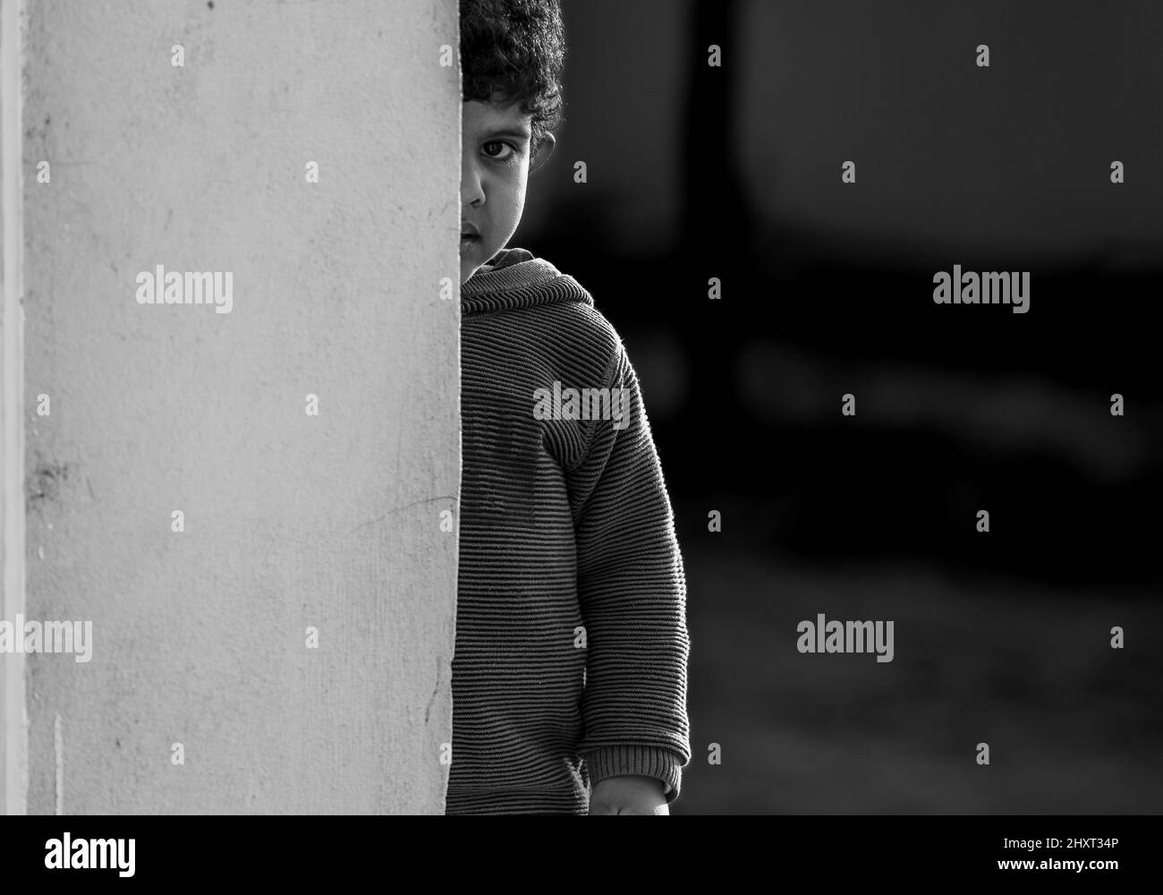 Grayscale shot of the little cute boy looking around the corner in the ...