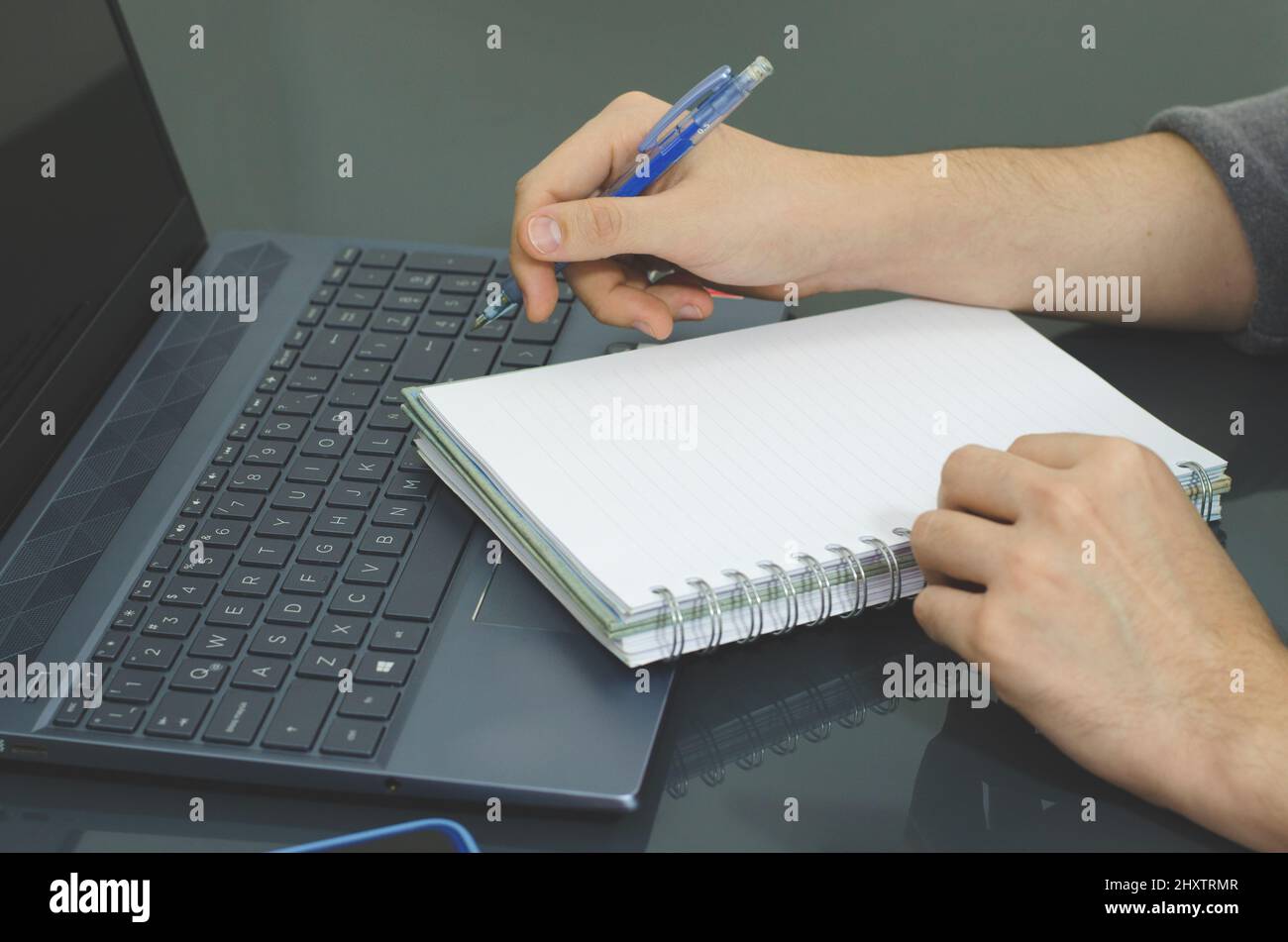 Shot of a person taking notes on a copybook, on a laptop working from ...