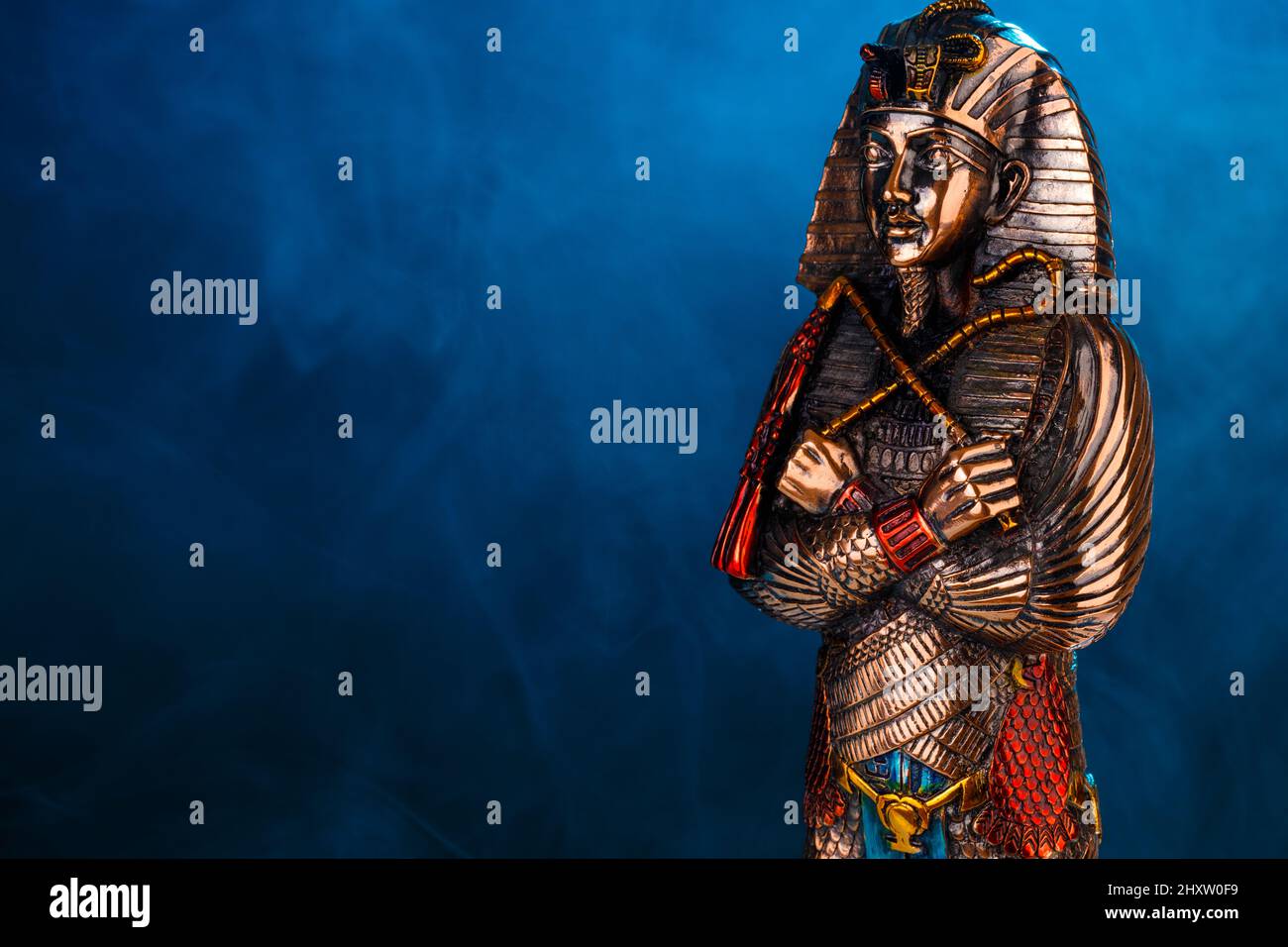 golden Egyptian pharaoh figurine in blue smoke on a black background ...