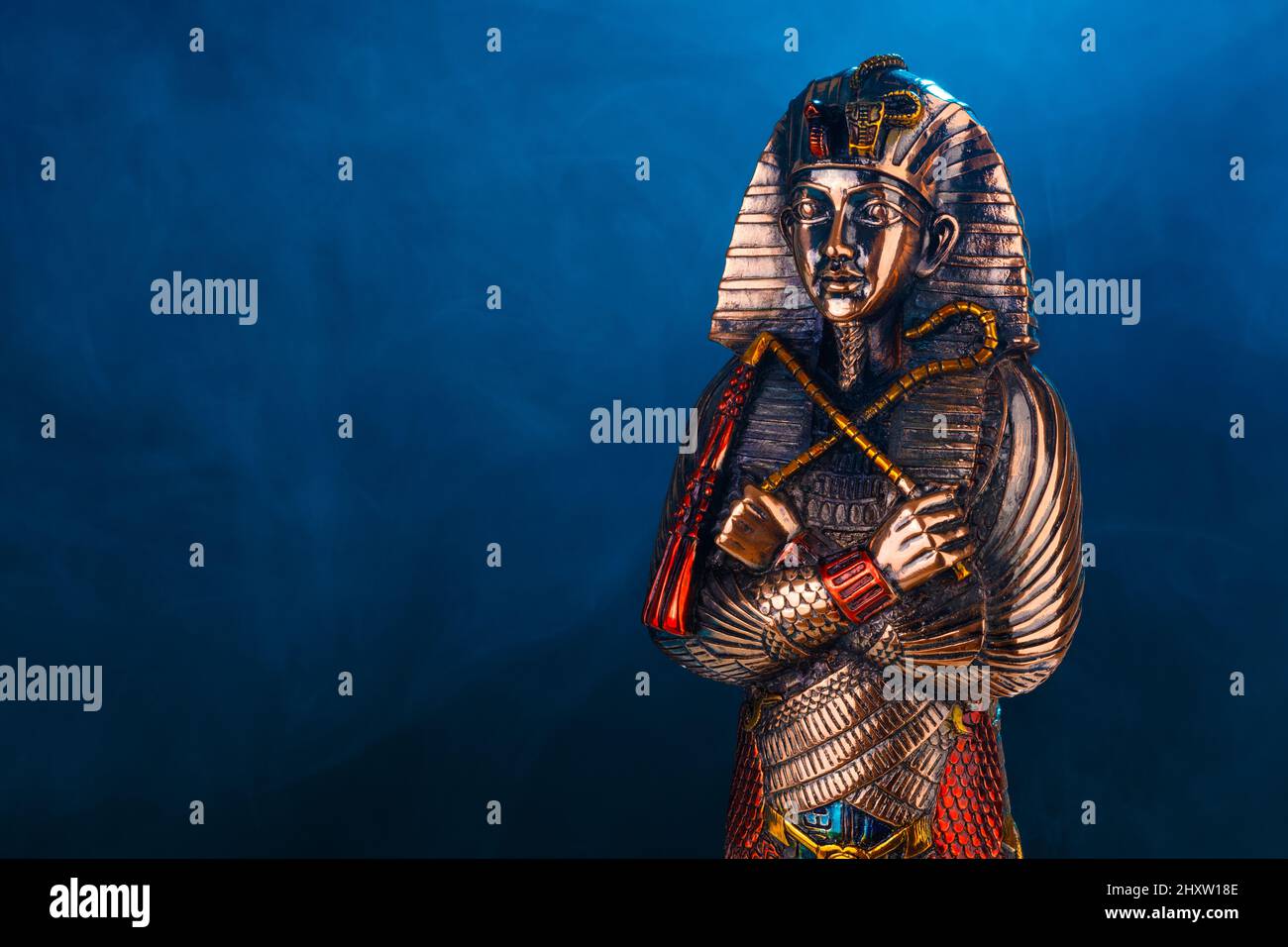 golden Egyptian pharaoh figurine in blue smoke on a black background ...