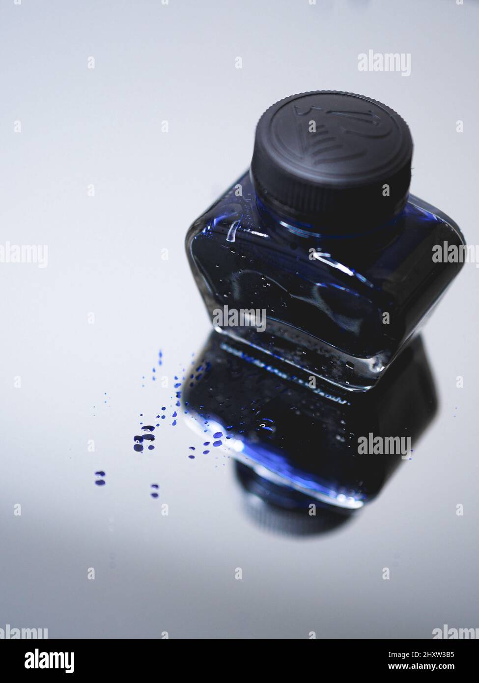 Vertical selective focus shot of an ink bottle on a mirror table and ...