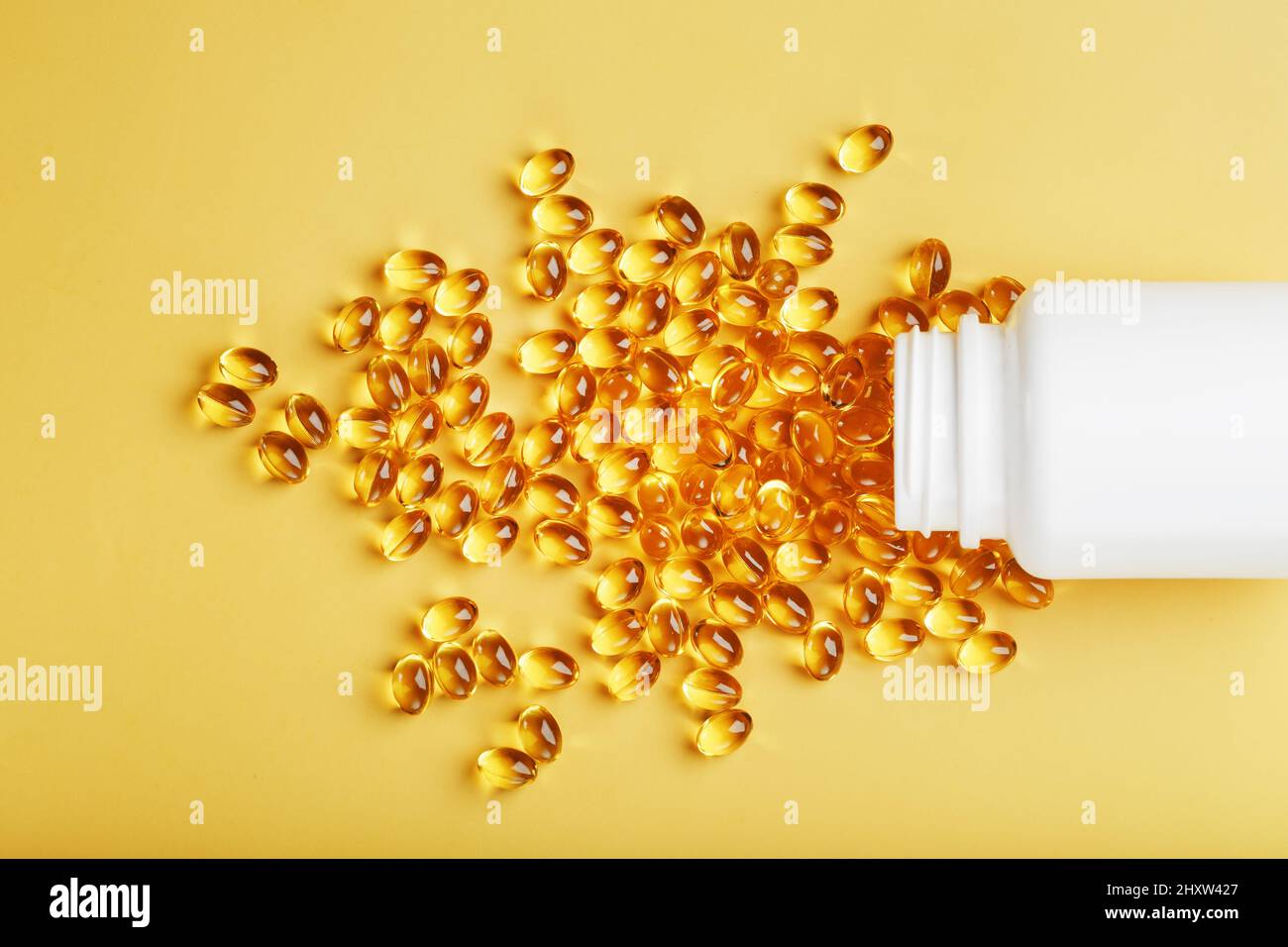 Gold Vitamin D3 capsules poured out of a jar on a yellow background ...