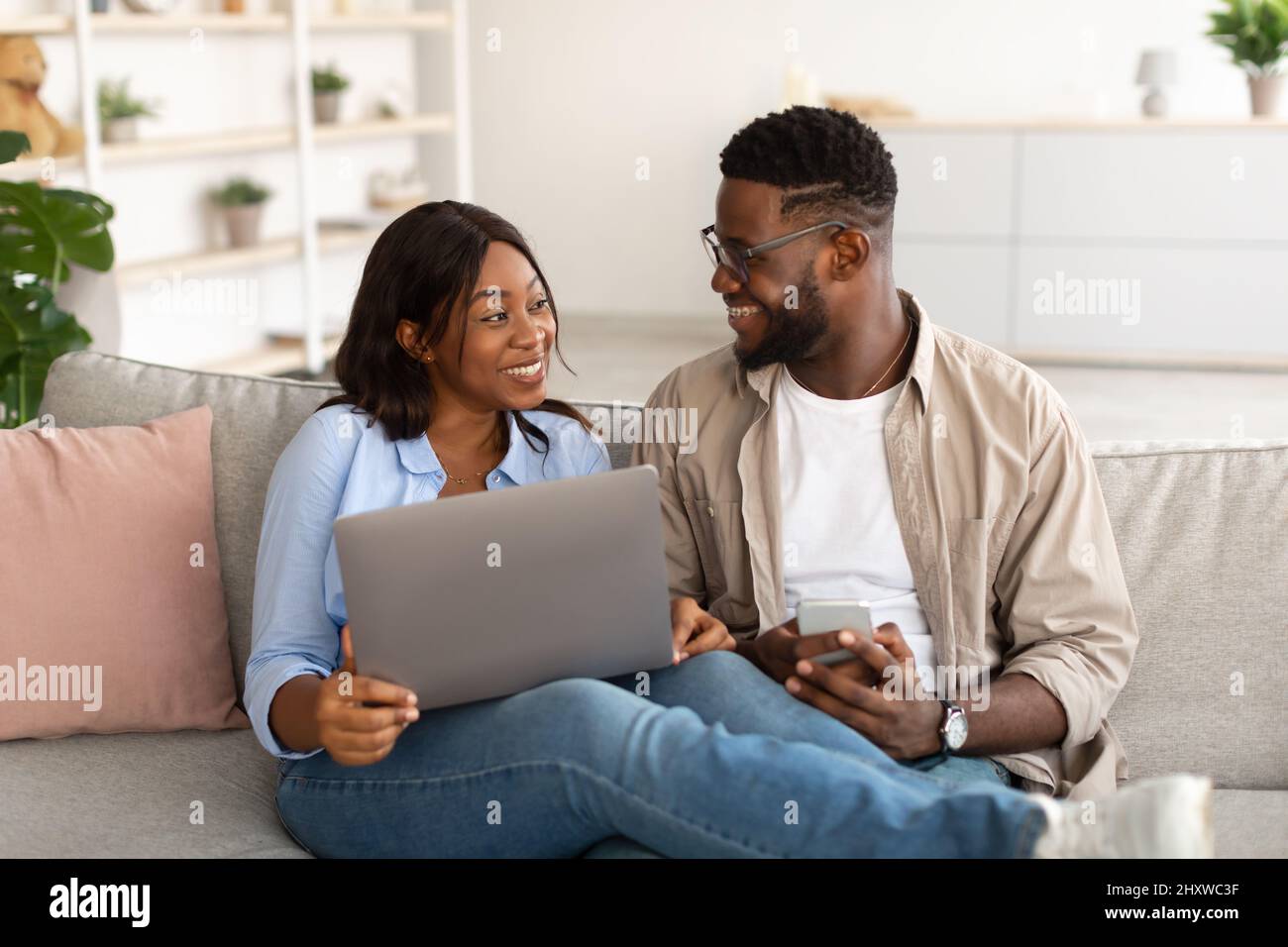 Happy black couple sitting on couch, using cellphone and pc Stock Photo ...