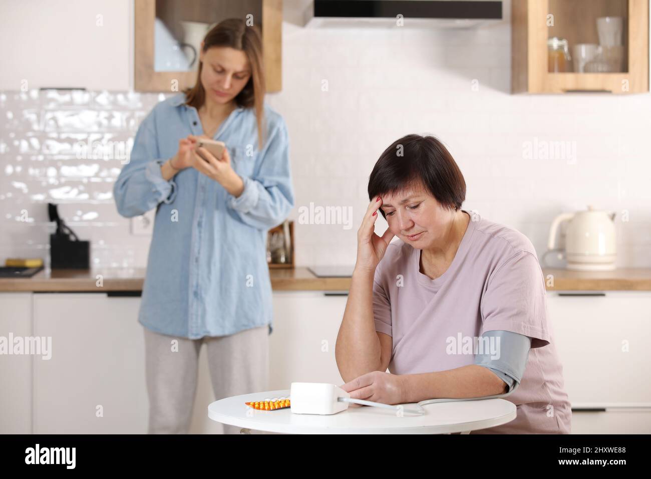 worried young woman calling doctor for her senior mother at home. sick ...