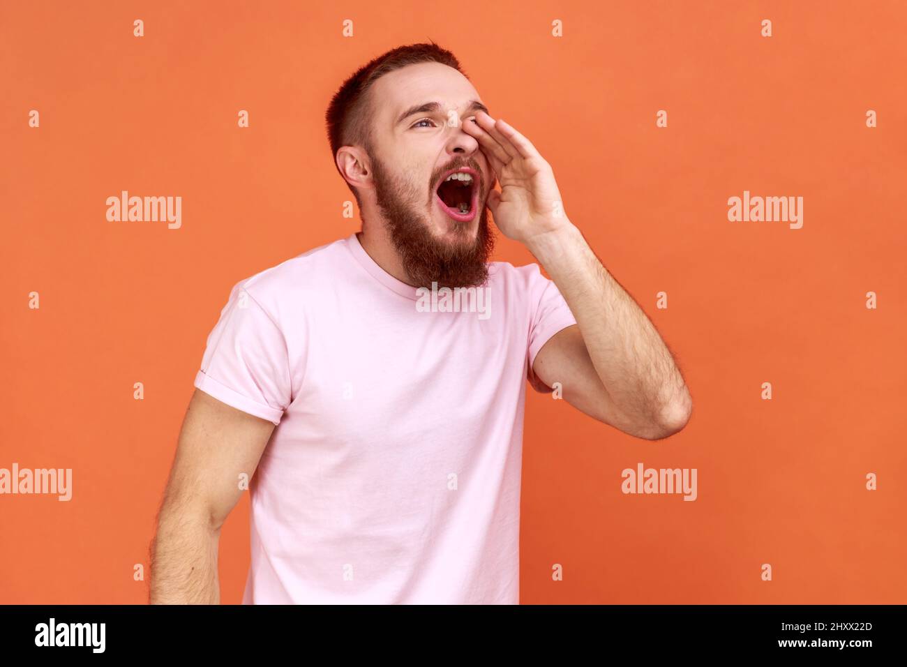 Side view of handsome bearded man loudly yelling, holding hand near ...