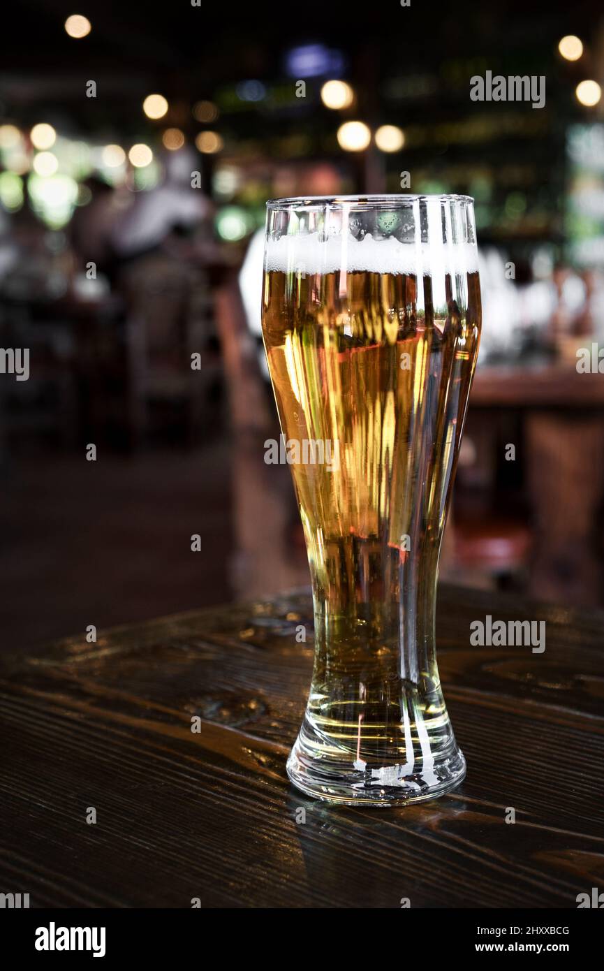 Glass of cold lager beer with foam on bar or pub desk. Blurred ...