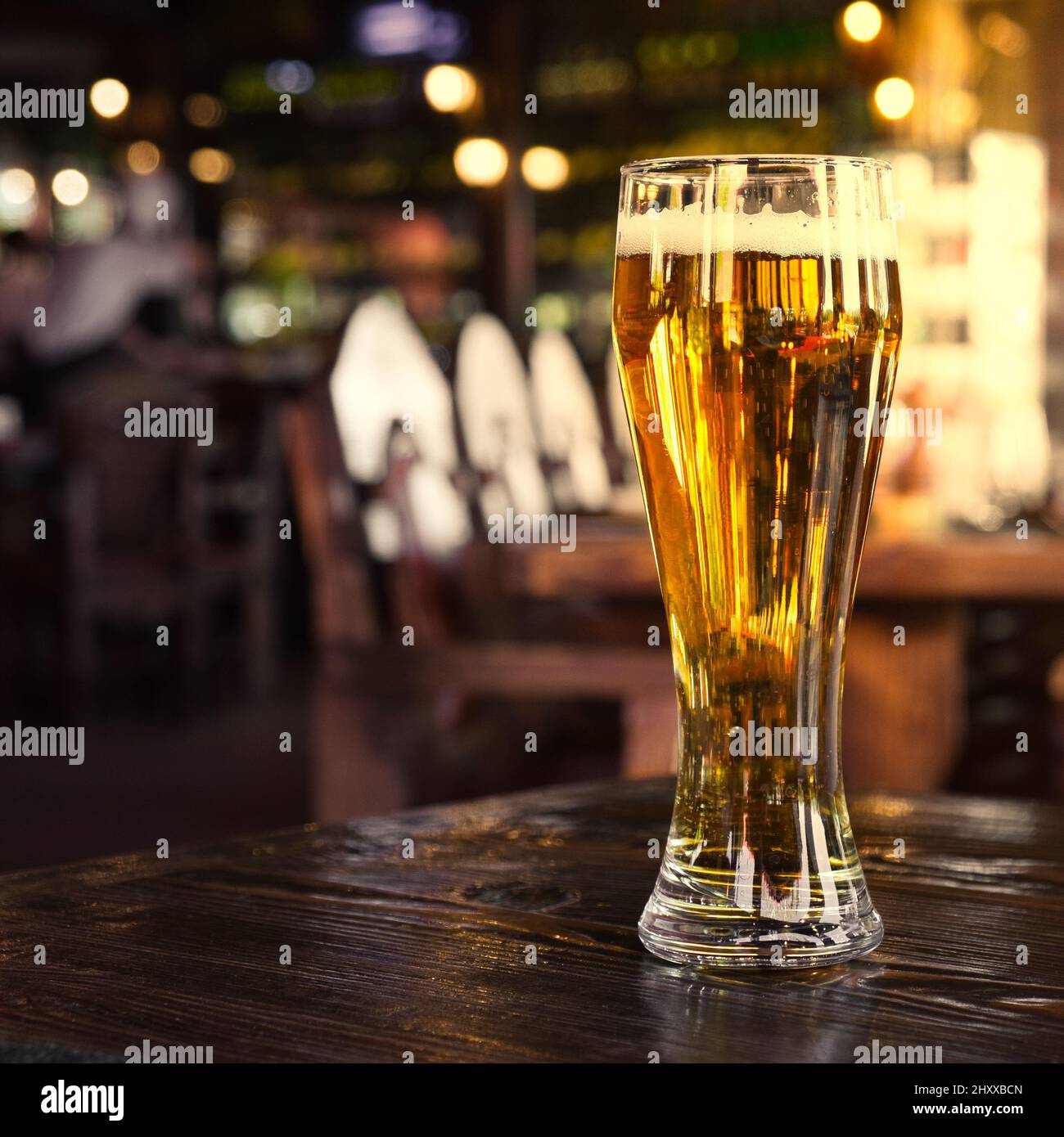 Glass of cold lager beer with foam on bar or pub desk. Blurred ...