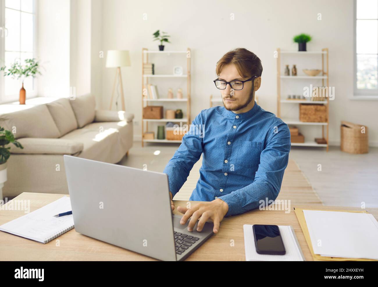 Serious young man sitting at his desk in home office and working on ...