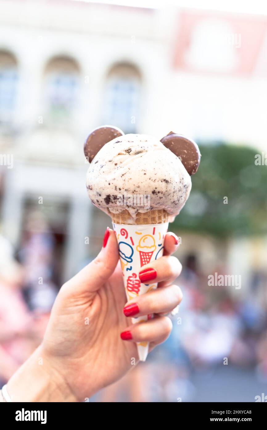 Vertical shot of a woman holding an ice-cream cone with mouse ears ...