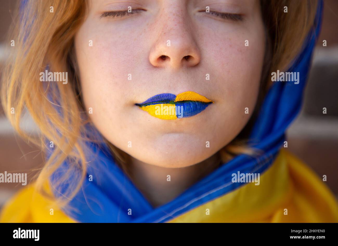 female face with closed eyes and painted yellow-blue lips close-up ...