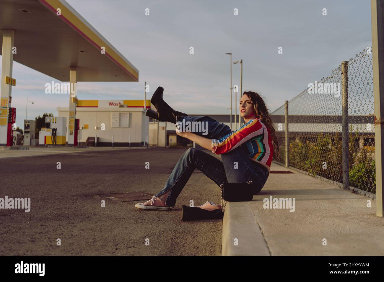 Caucasian female sitting on a sidewalk near a gas station and changing ...