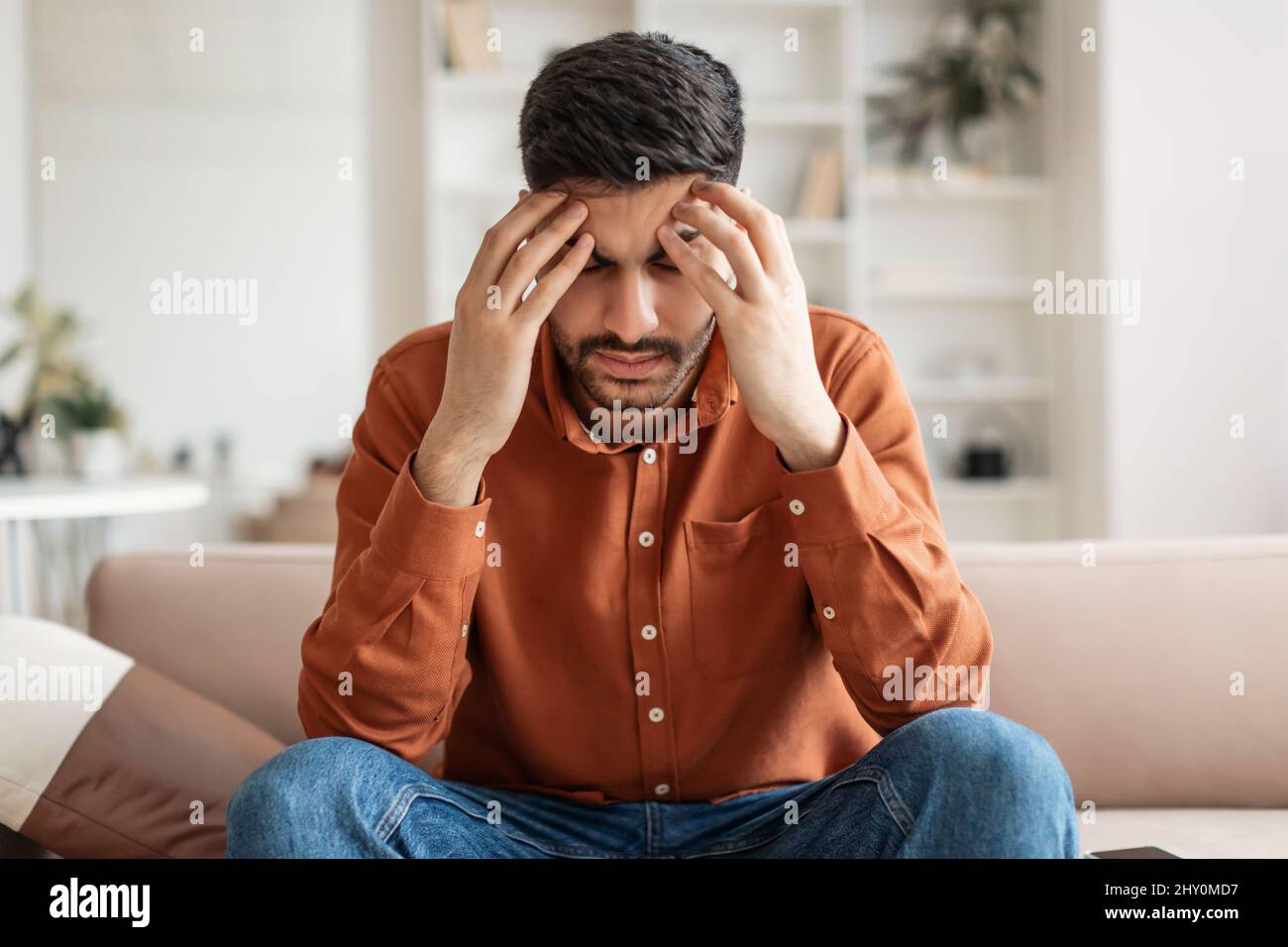 Stressed Arab man sitting on couch and thinking Stock Photo - Alamy