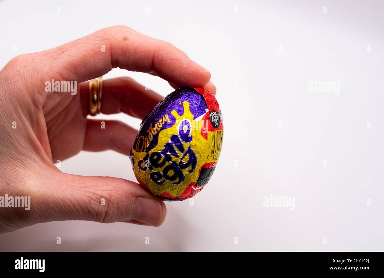 Human hand holding a Cadbury Crème Egg against a plain white background ...