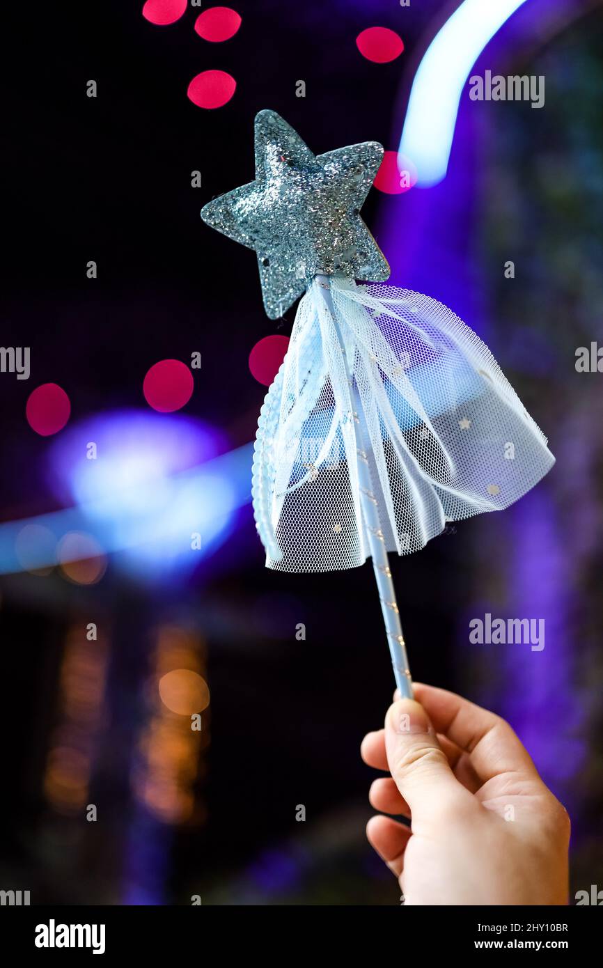 Vertical closeup of a kid's hand holding a silver star toy on a stick ...
