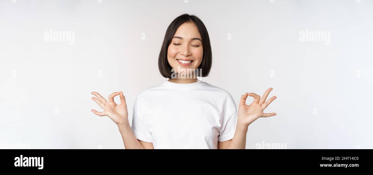 Portrait of young asian woman meditating, smiling pleased and practice ...