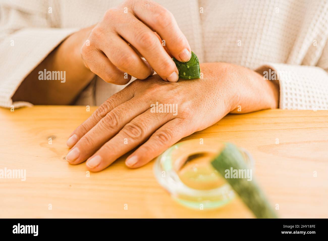Crop anonymous female rubbing hand with green aloe vera while sitting ...