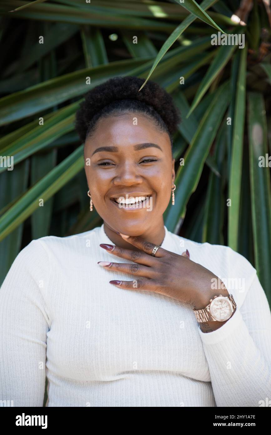 Positive African American female touching neck while standing near lush ...