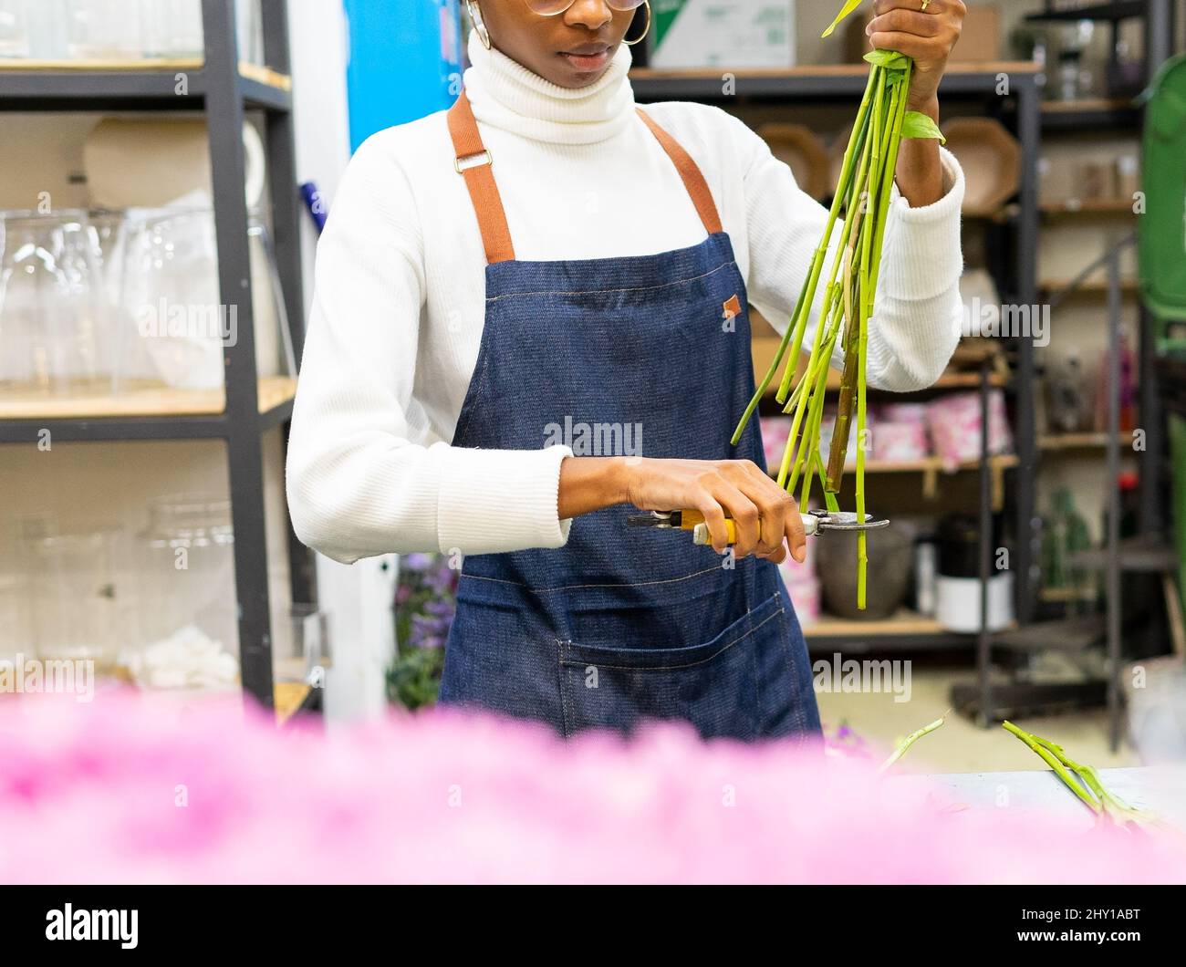 Crop anonymous florist in apron cutting green stalks of flowers with ...