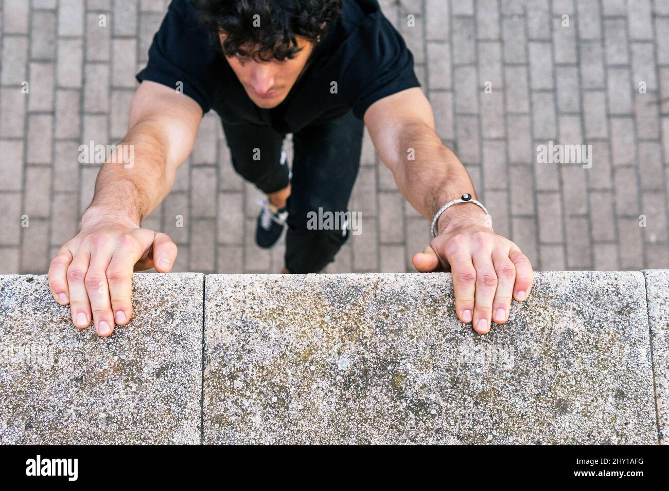 From above male athlete in black clothes holding hands on stone border ...