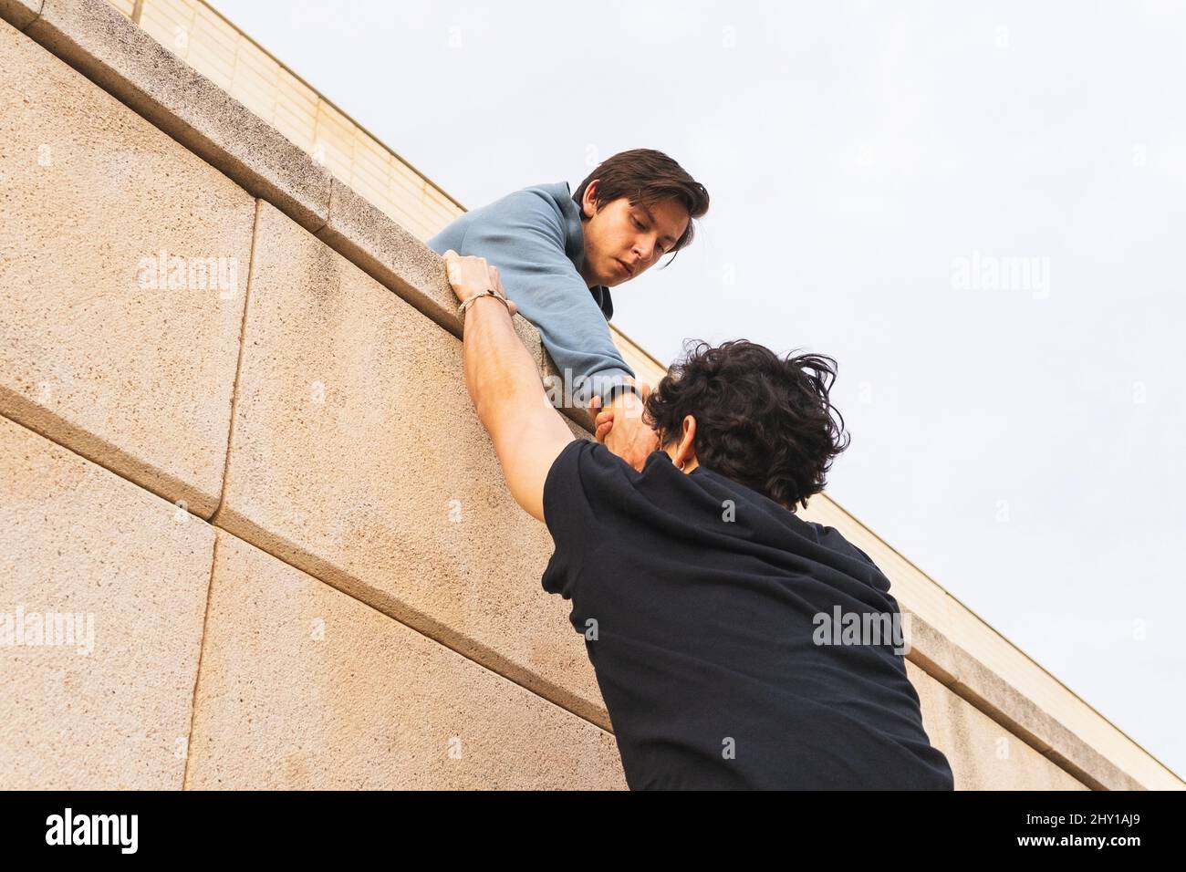 From below man in gray clothes on roof holding hand of man in strong ...