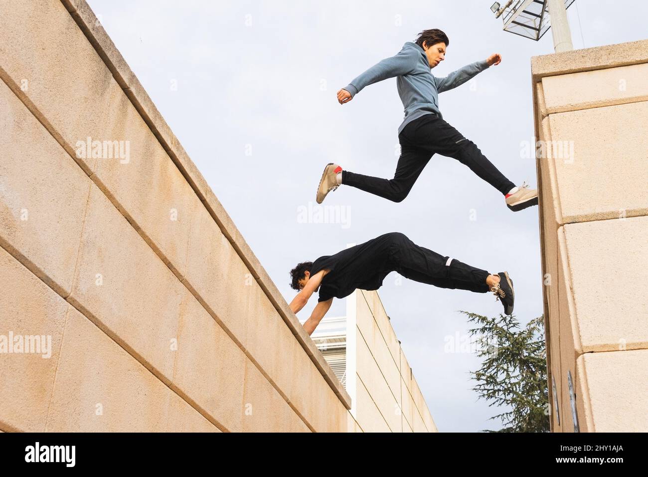 From below side view of full length active men jumping over border roof ...