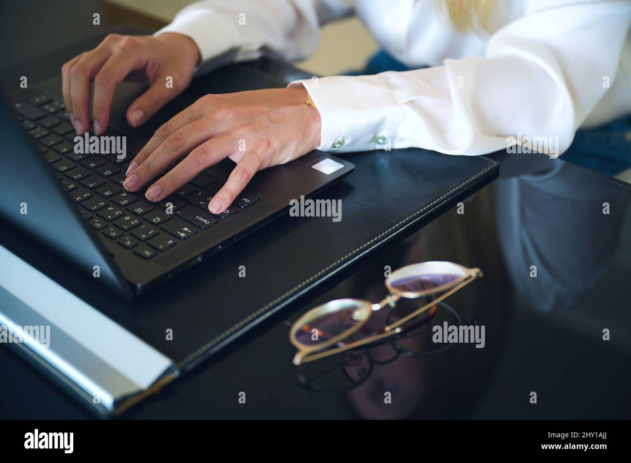 Crop anonymous female employee browsing netbook while working at table ...