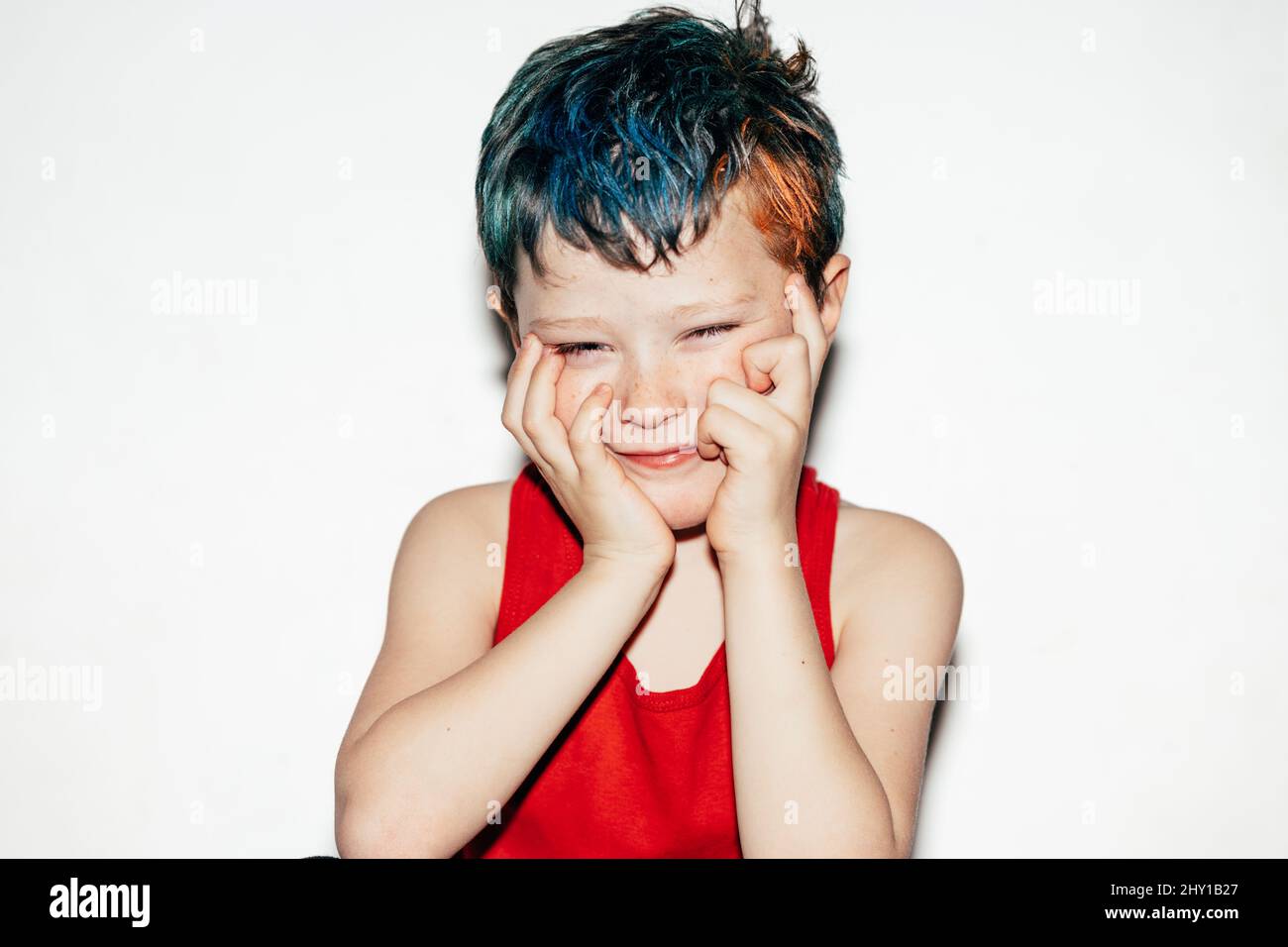 Rebellious boy with dyed hair looking away and touching face with hands ...