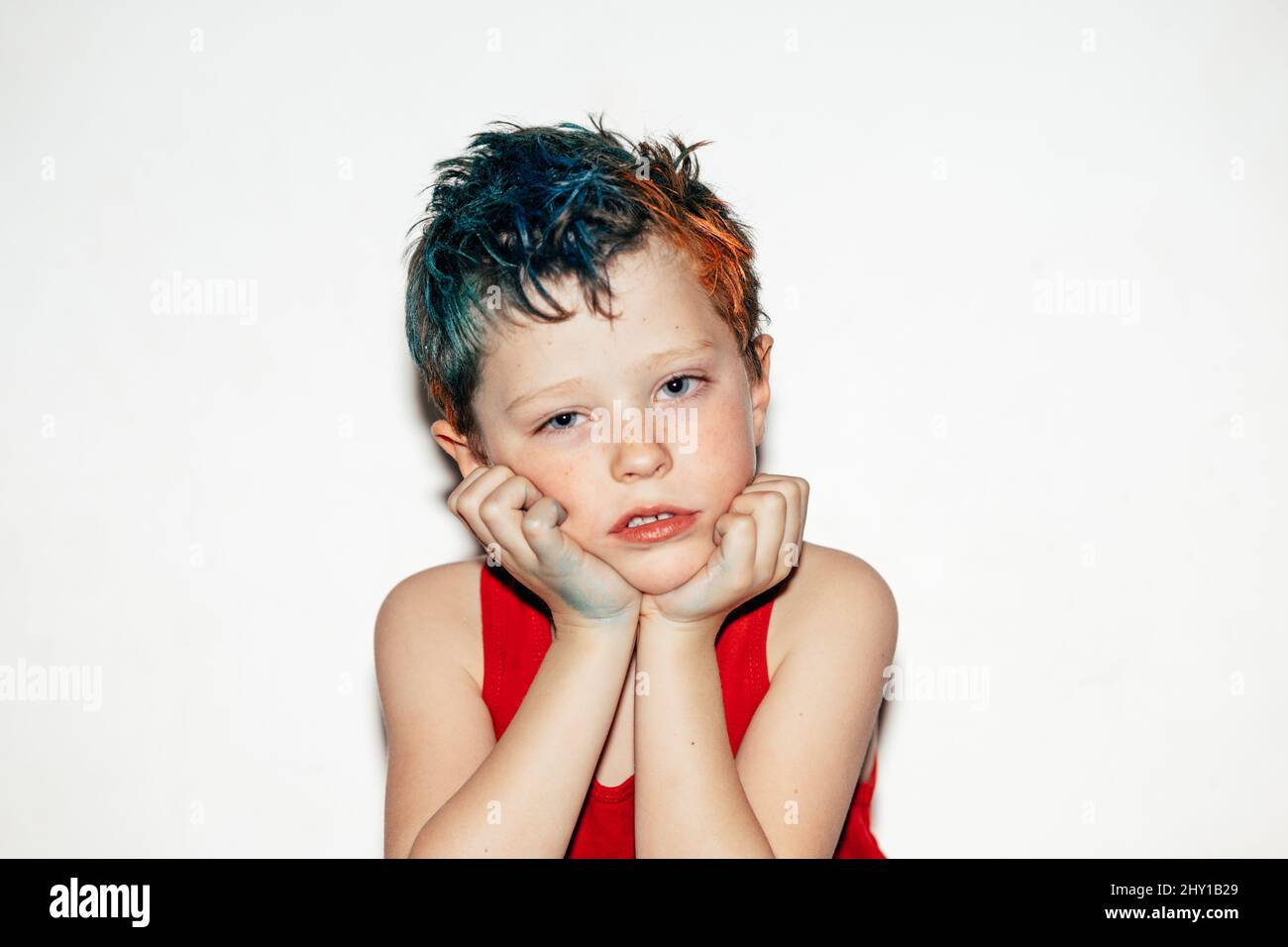 Rebellious boy with dyed hair looking at camera with serious face while ...