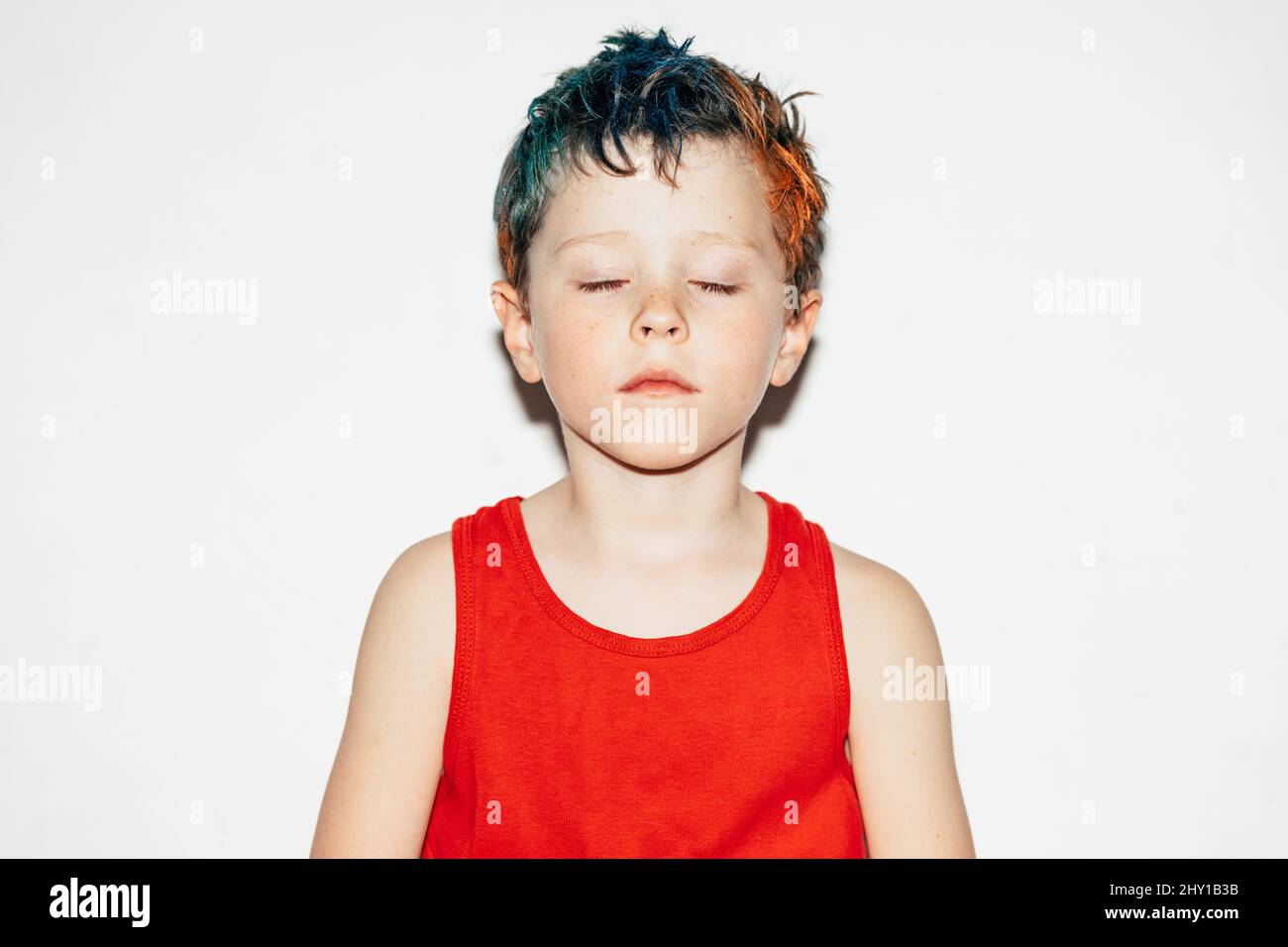 Mischievous boy with colorful dyed hair and closed eyes on white ...