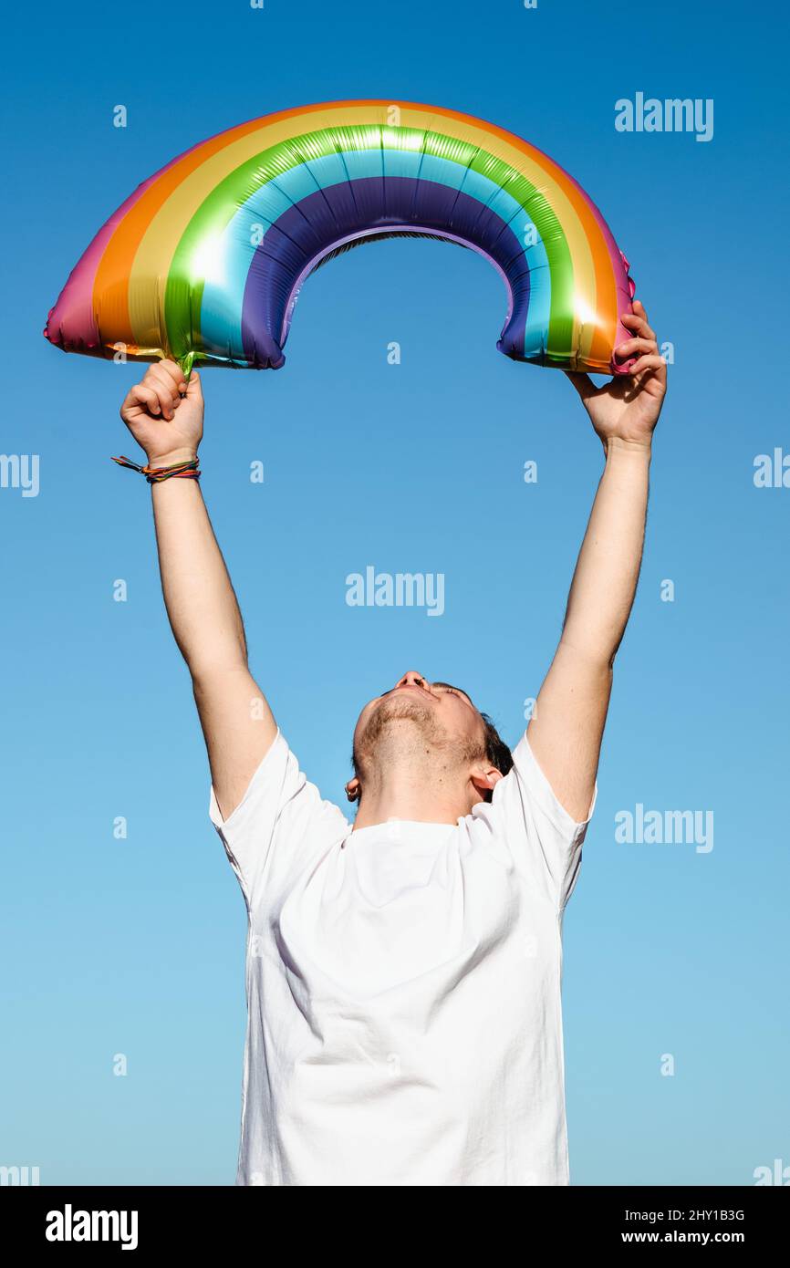 Joyful transgender male with rainbow shaped balloon with LGBT symbol in ...