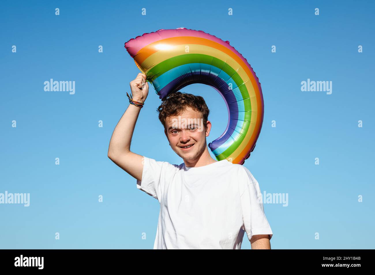 Joyful transgender male with rainbow shaped balloon with LGBT symbol in ...