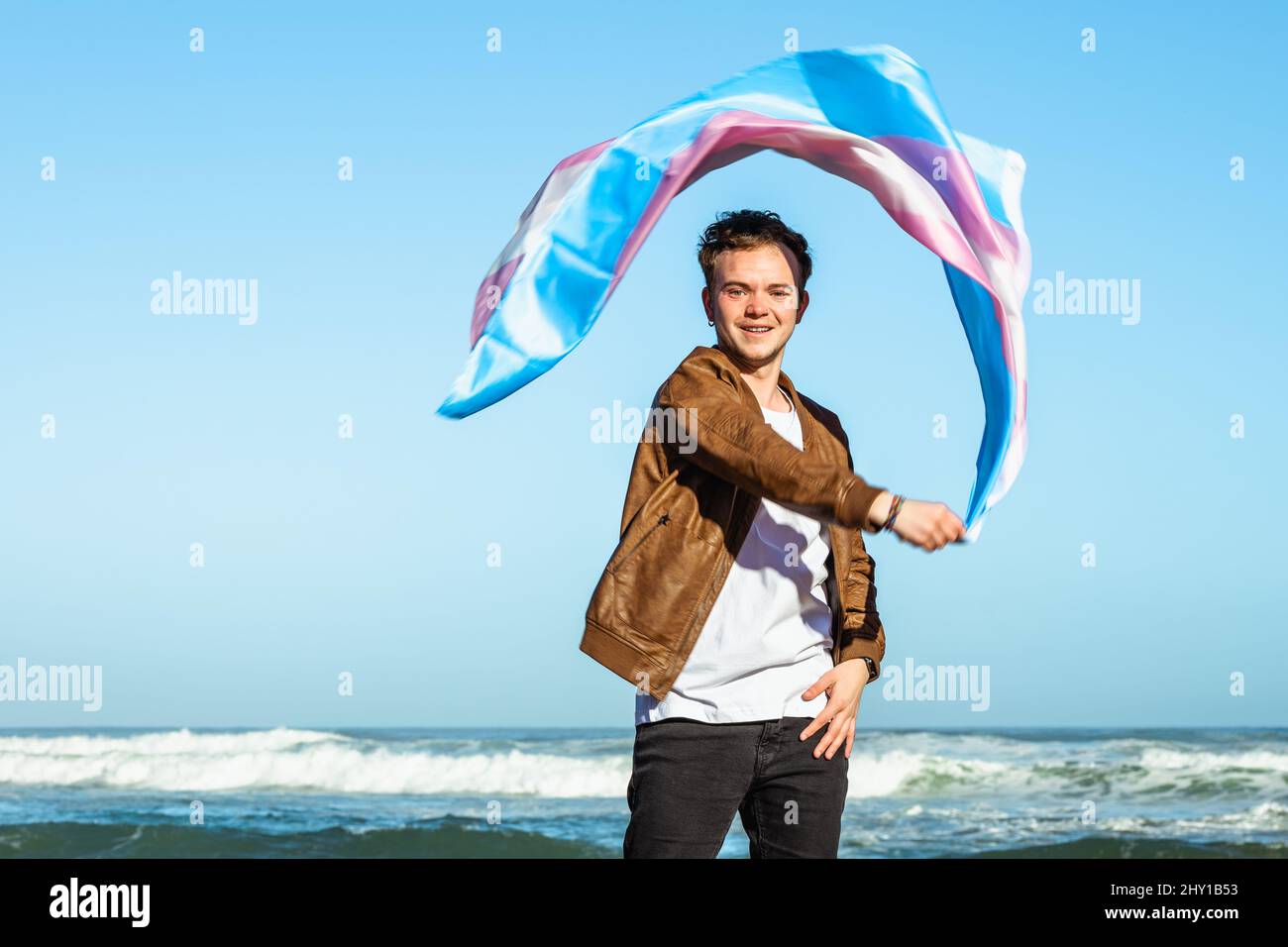 Positive transgender male with colorful flag standing on coast with ...