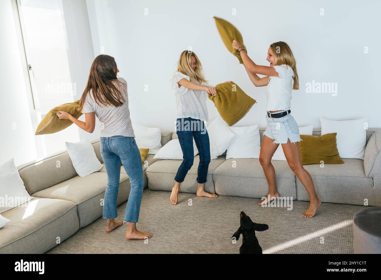 Full body of happy barefoot female friends fighting with pillows while ...