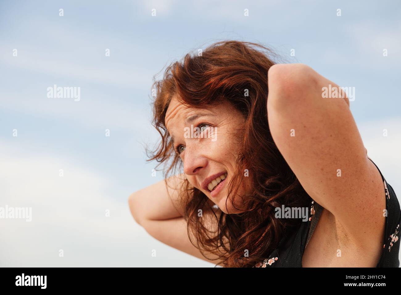 Positive female in black sundress touching hair while standing against ...