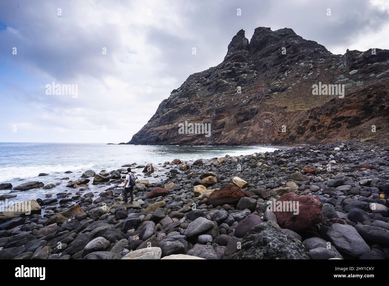 Back view of distant unrecognizable traveler standing on stony shore ...