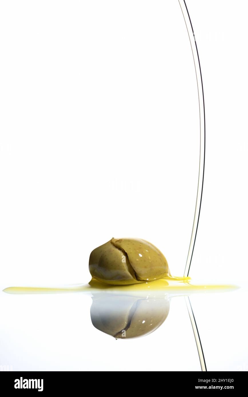 Healthy green oval olive with cut on spilled yellow oil placed on ...