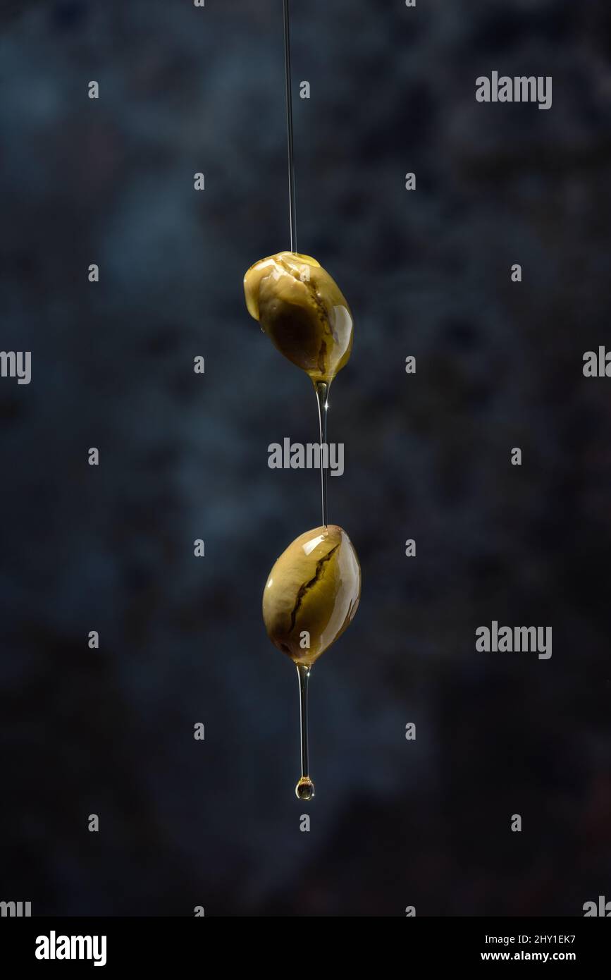 Soft focus of oil dripping from green healthy oval shaped whole olives ...