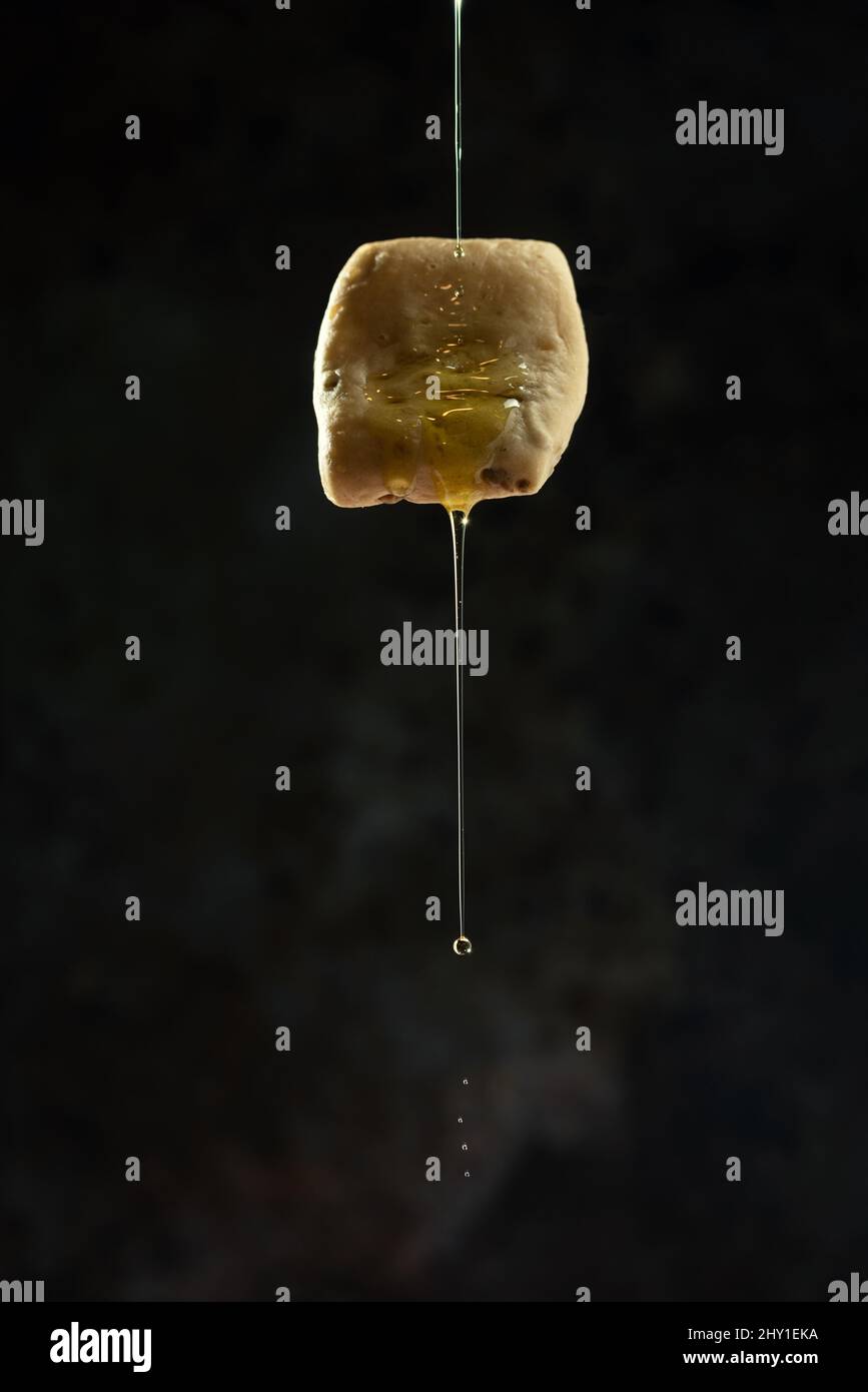 Thin stream of olive oil dripping from square piece of falling dough ...