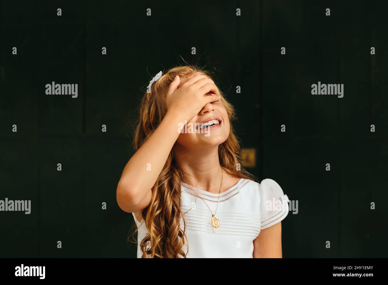 Positive young female in First Communion dress with long hair and hand ...