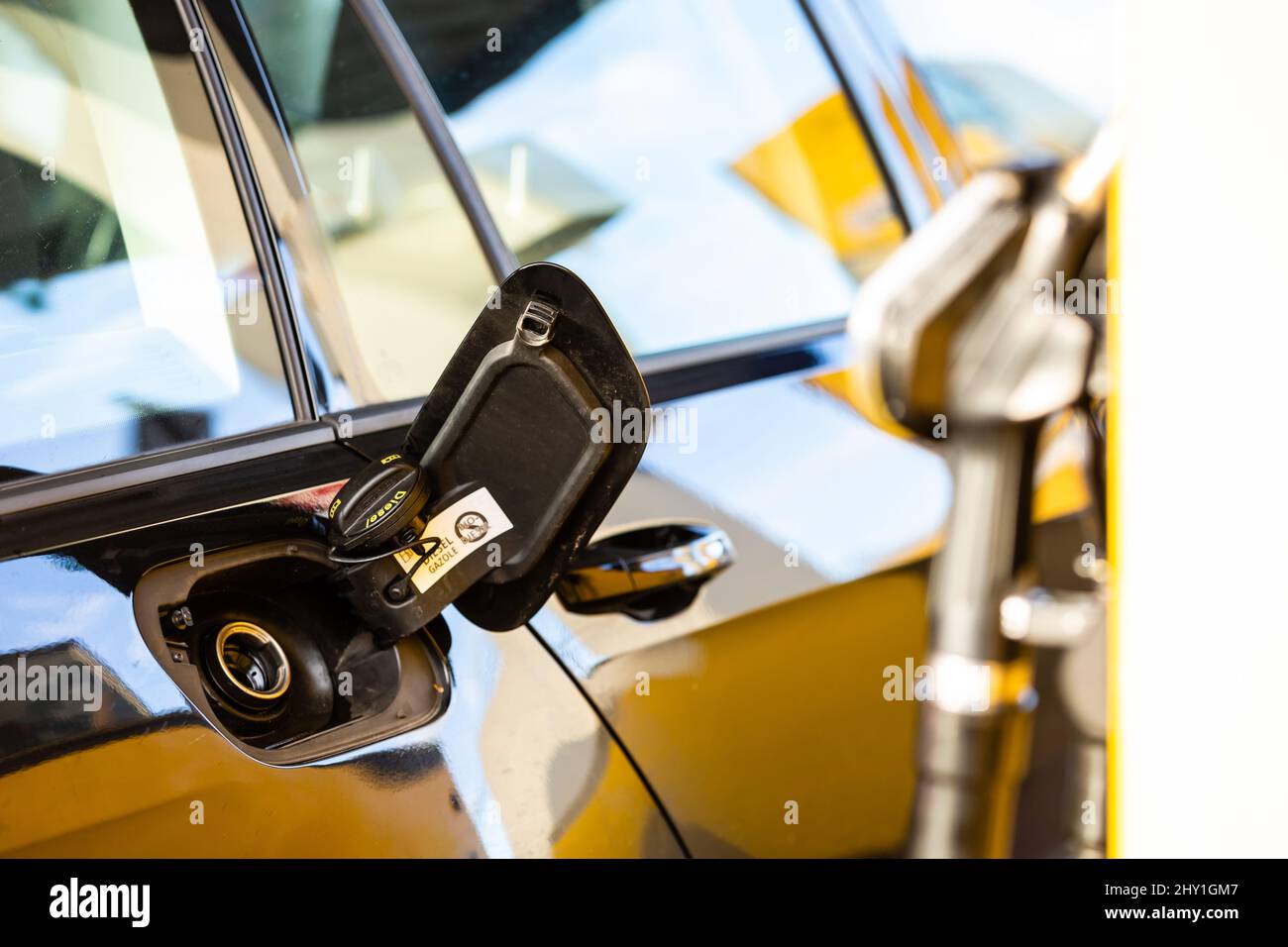 Closeup of fuel nozzle at a gas station with fuel tank cap on a car ...