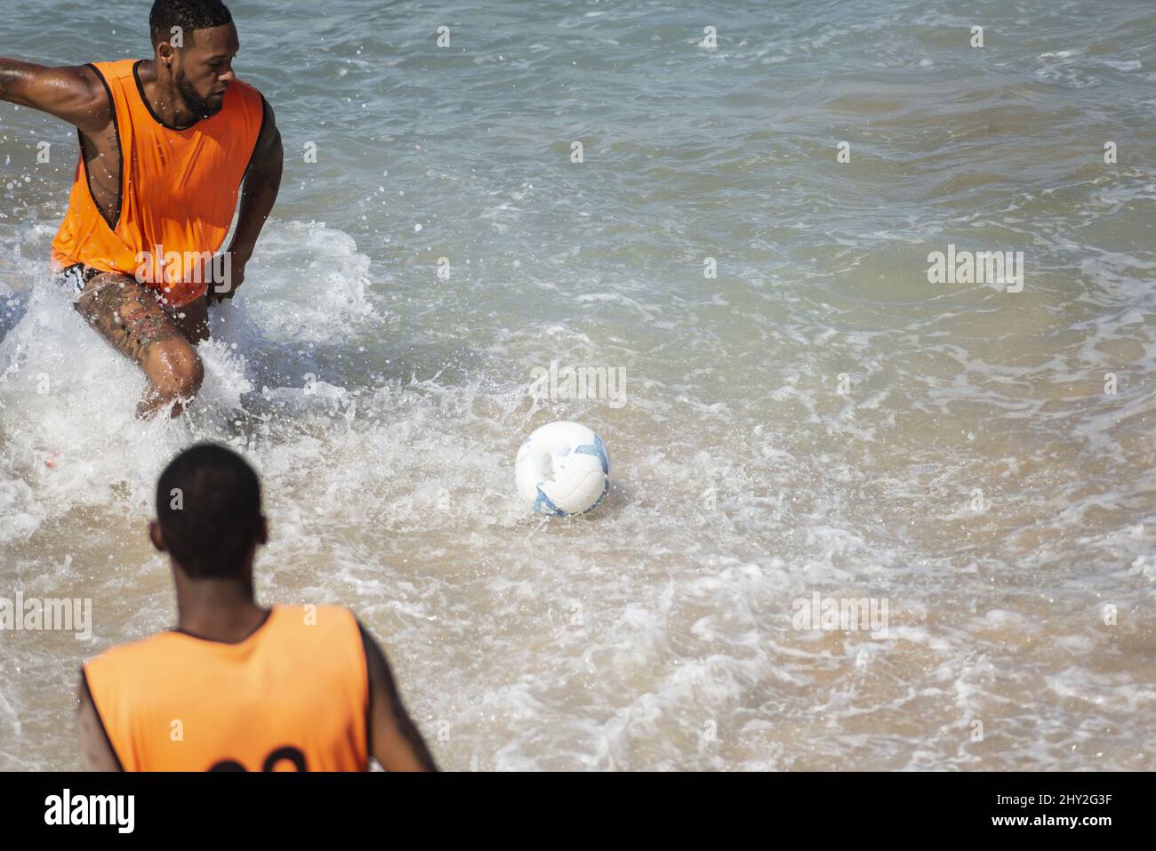 Two black men trying to kick the ball in the water at Farol da Barra ...